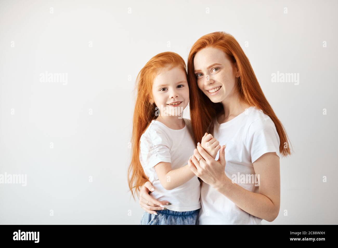 Close-up portrait of smiling mother hugging cute four year old daughter ...