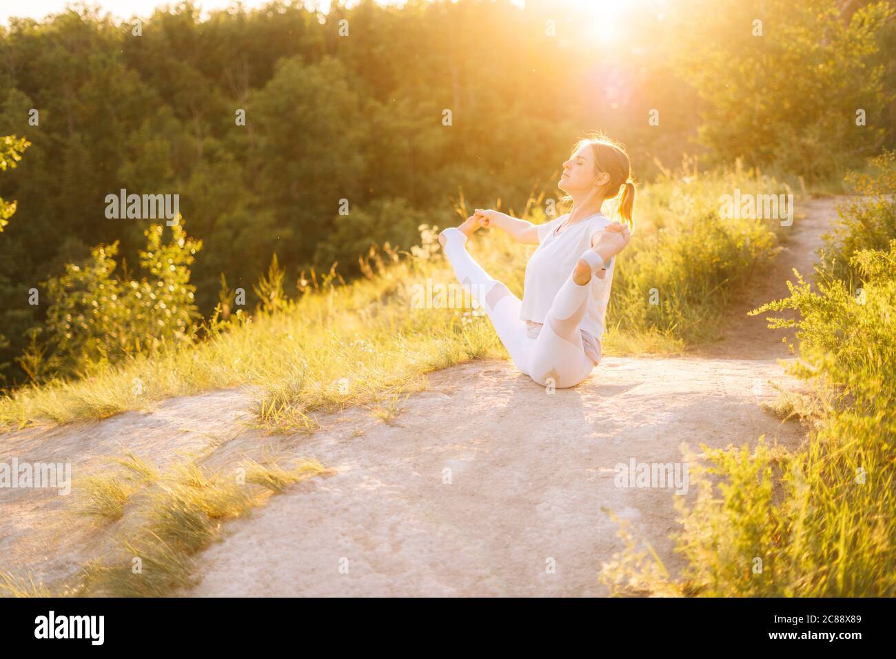 Young fit woman performing yoga posture Boat with Toe Hold, outside ...