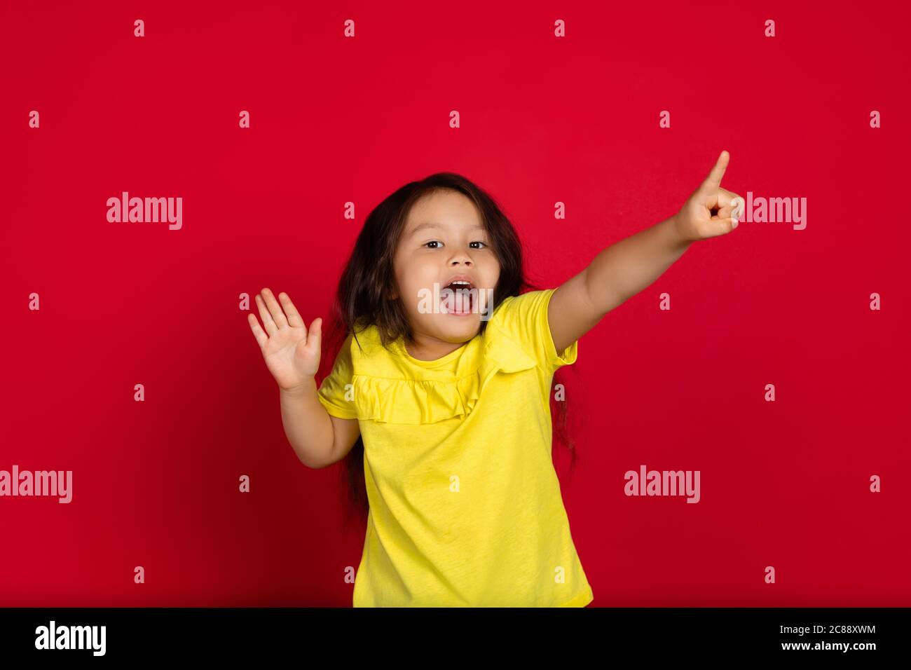 Pointing. Beautiful little girl isolated on red background. Half-lenght ...