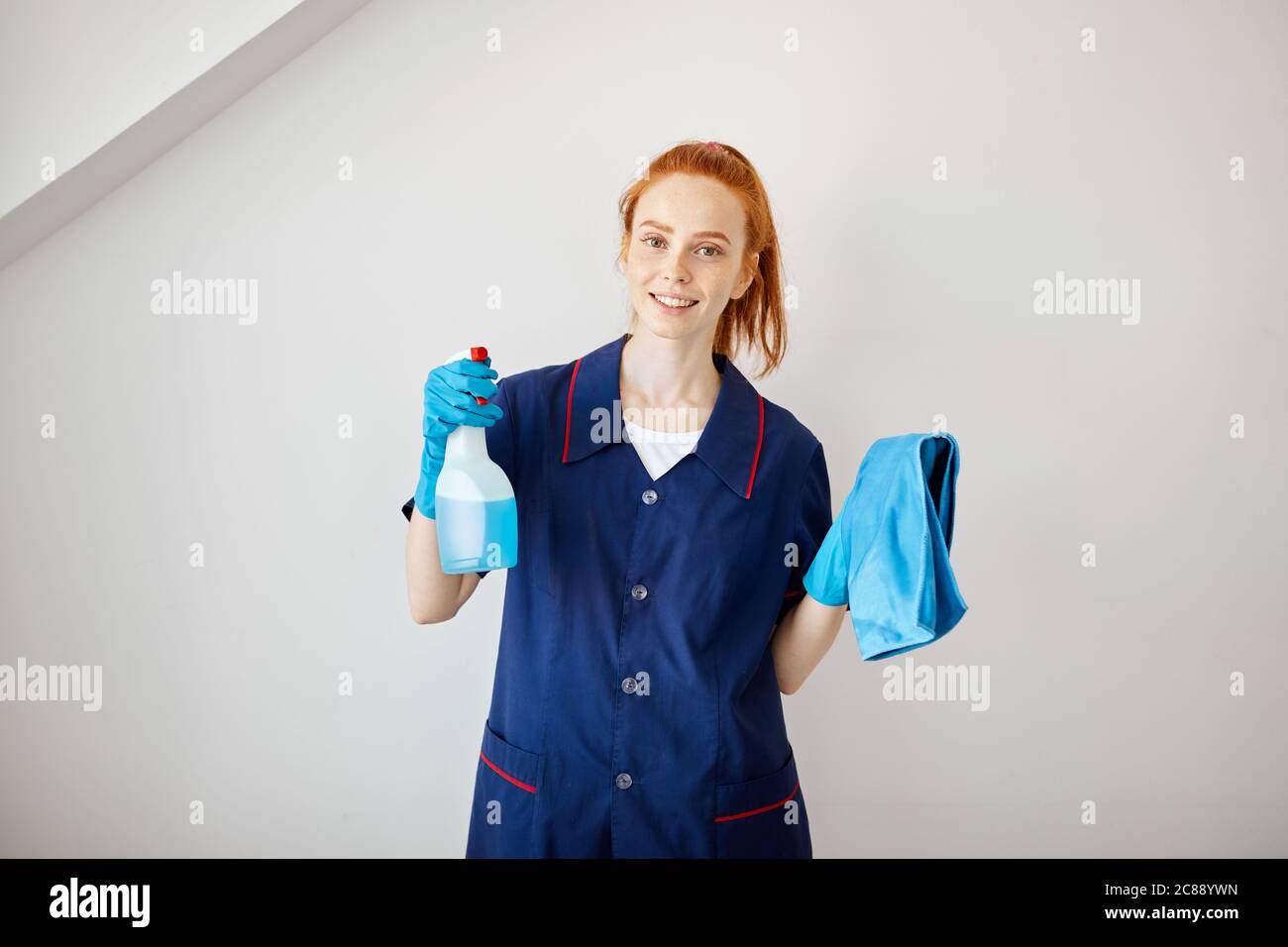 Positive pretty young cleaning lady in blue uniform holds cleaning ...