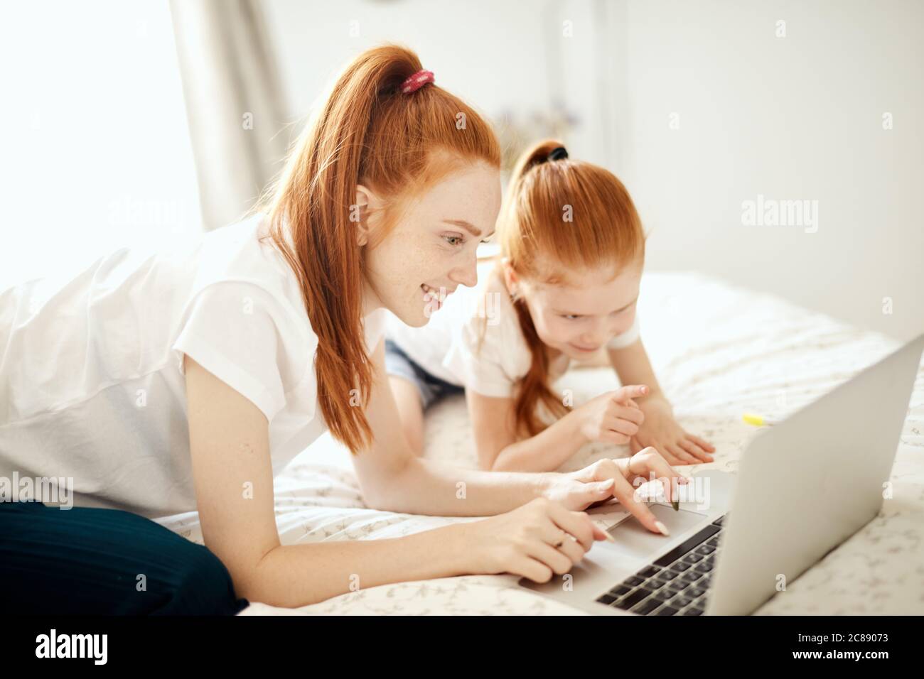 Cute little red-haired girl spend time with mom, browsing computer or ...