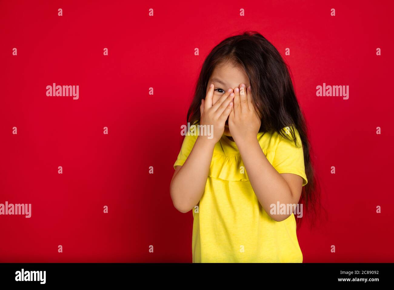 Scared hiding face with hands. Beautiful little girl on red background ...