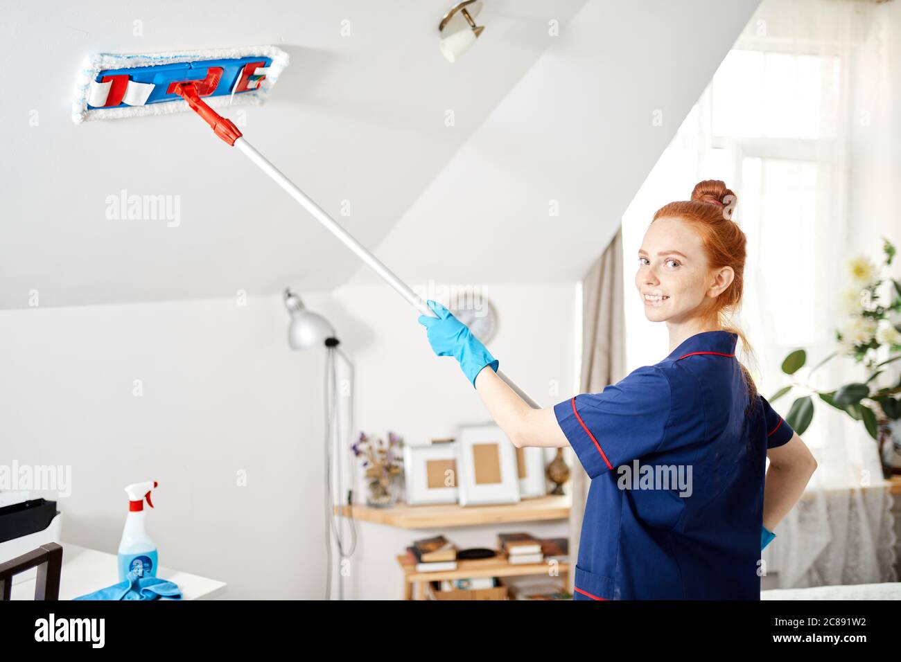 Pleased happy redhead maid woman holding mop pile, cleaning ceiling at ...