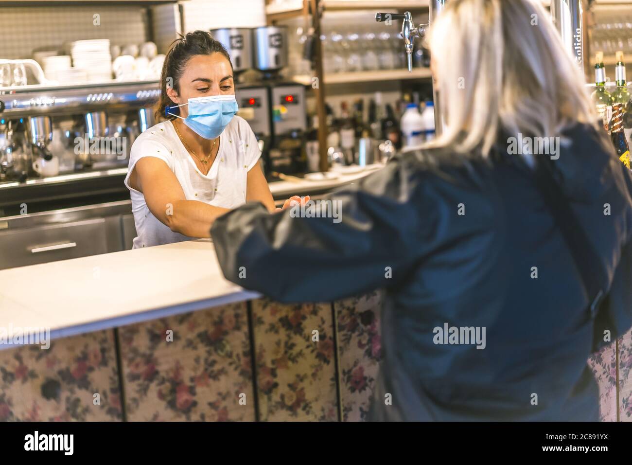 Caucasian brunette waitress with a face mask working at the bar serving ...