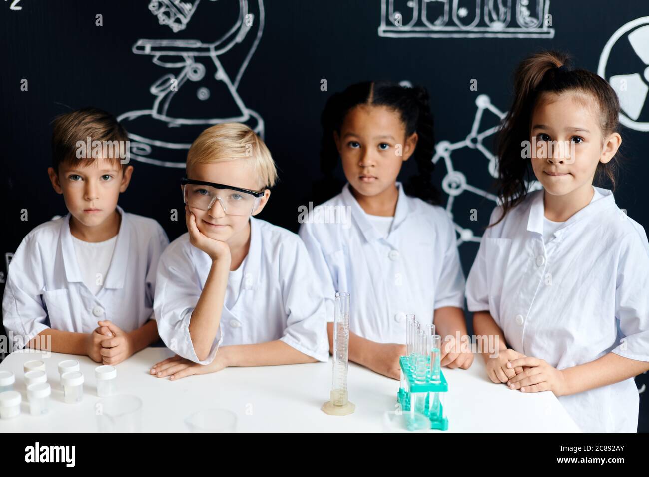 Cute elementary schoolkids looking at camera while standing at desk at ...