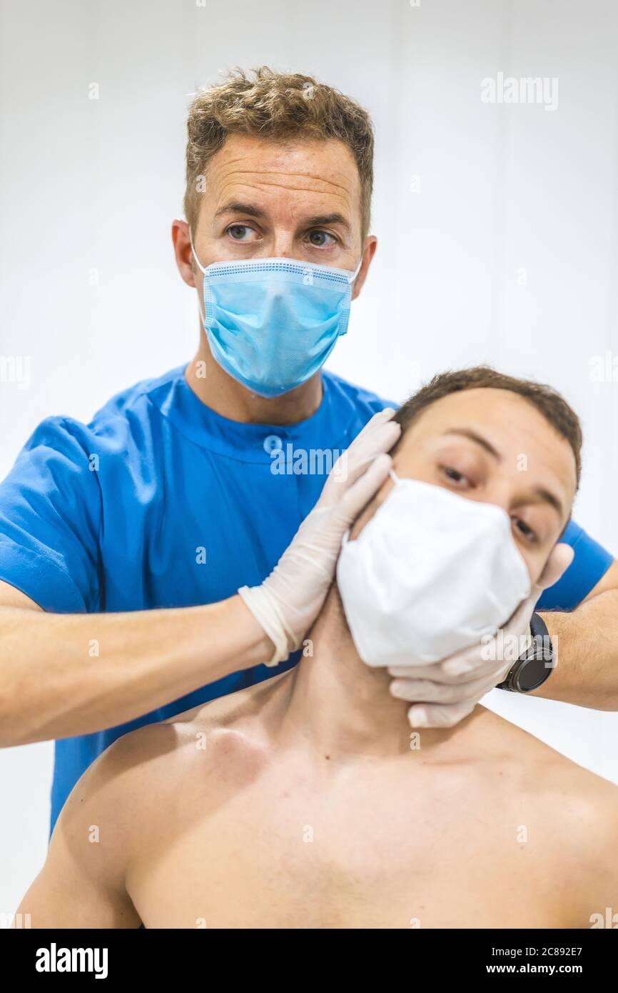 Doctor with a mask helping his patient with neck problems Stock Photo ...
