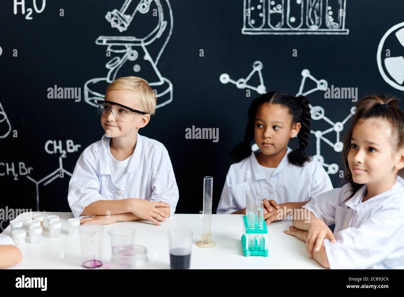 Multiethnic group of 7 years old kids in white lab coats doing a ...