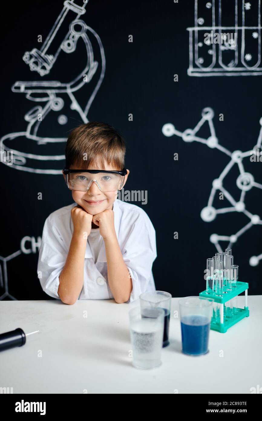Little boy scientist in lab coat, wearing safety eyeglasses, looking at ...