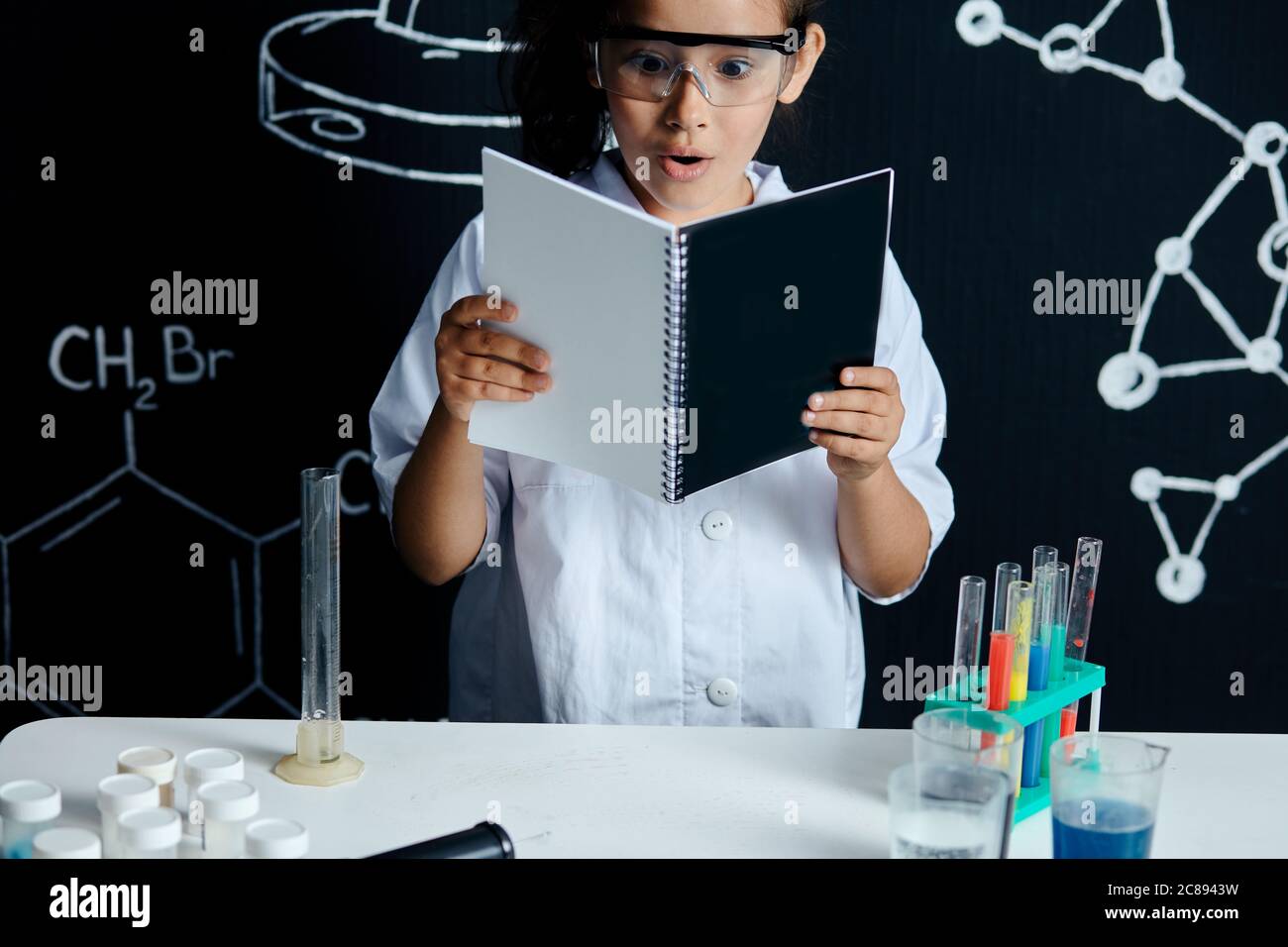 Little cute girl in white scientist coat reading notes, standing at ...