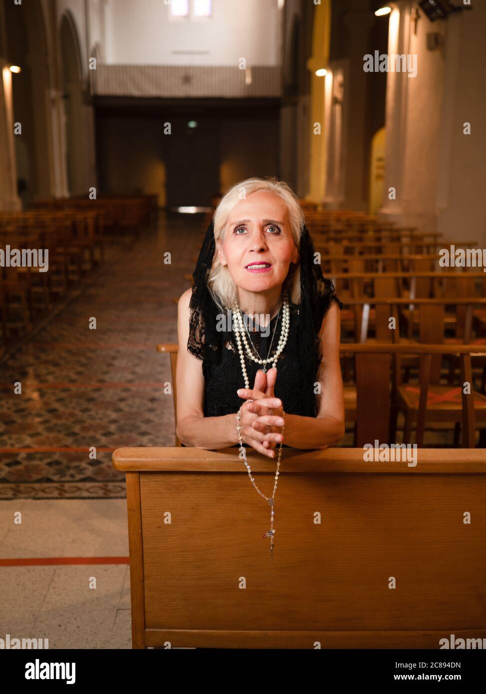 Vertical portrait of a mature woman sitting and praying in a church ...