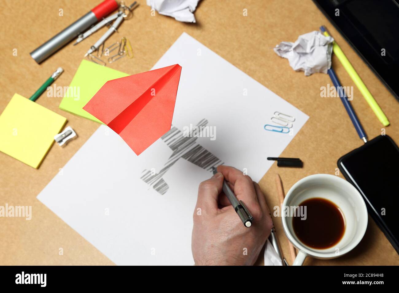 red paper plane flying over office desk, sketch of plane underneath ...