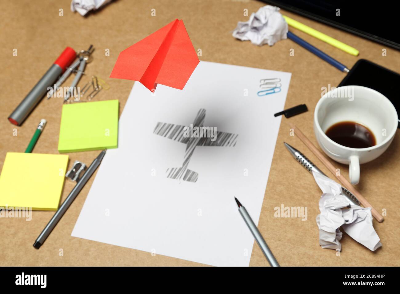 red paper plane flying over office desk, sketch of plane underneath ...