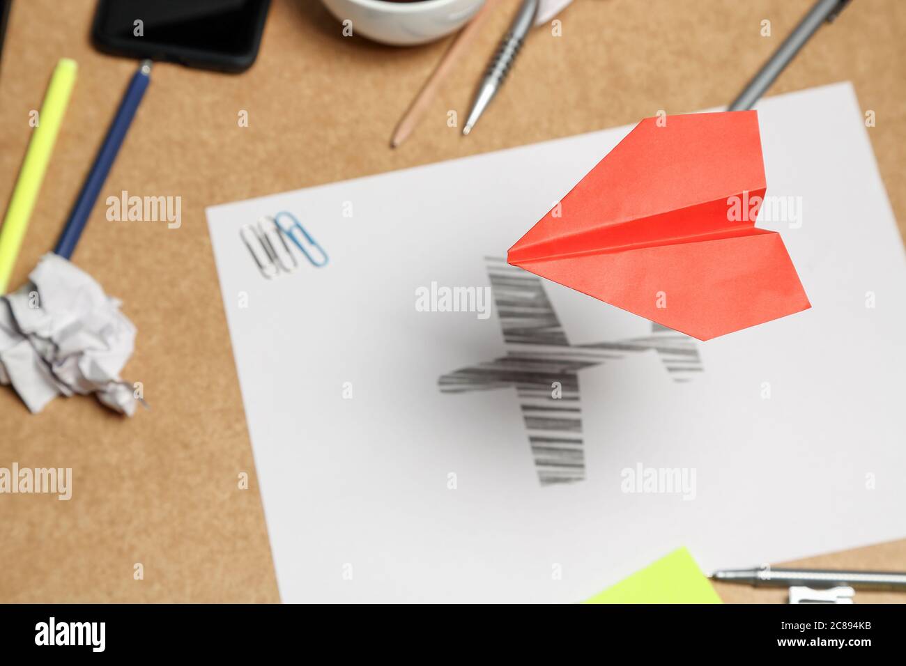 red paper plane flying over office desk, sketch of plane underneath ...