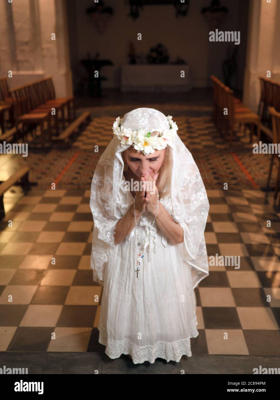 Vertical portrait of a woman kneeling and praying in a church with a ...