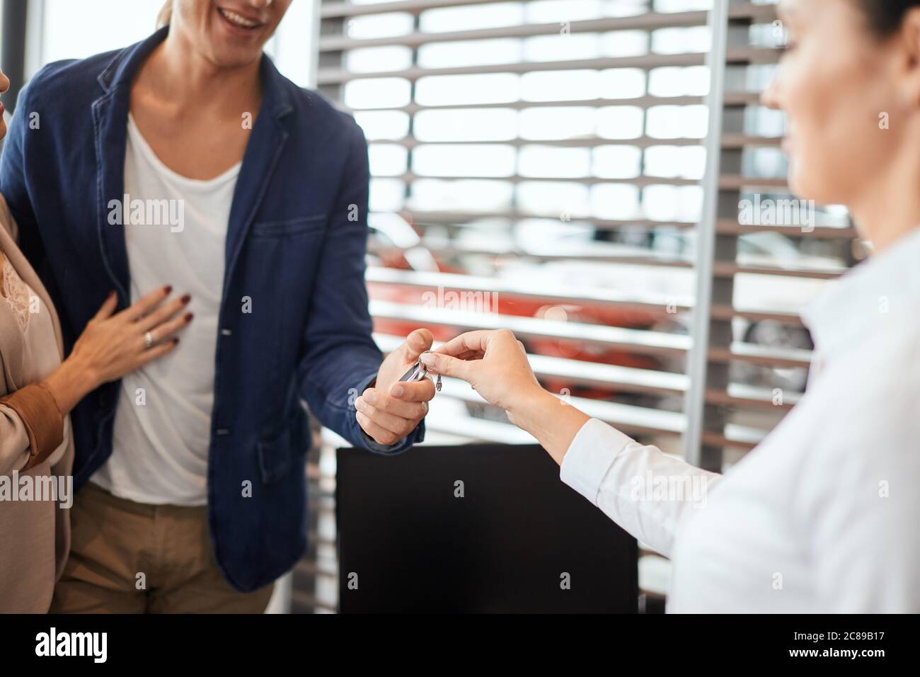 New car owners. Happy young couple receiving car keys from a salesman ...