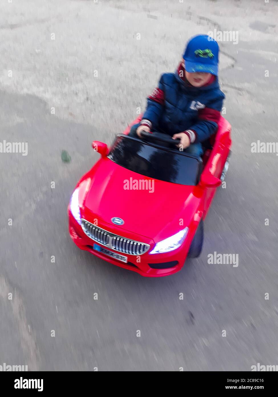 Little white boy of three years in a red children's electric car rides ...