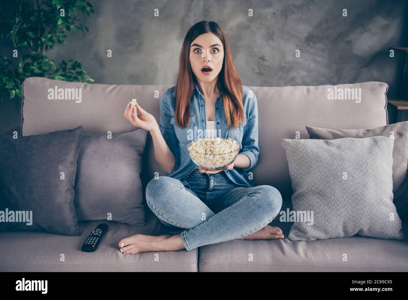 Portrait of astonished girl sit divan legs crossed folded eat popcorn ...