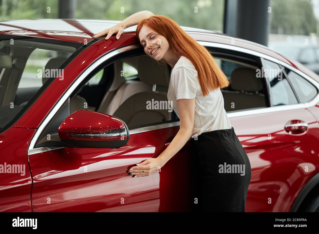 Emotional young woman embracing her new automobile at the dealership ...