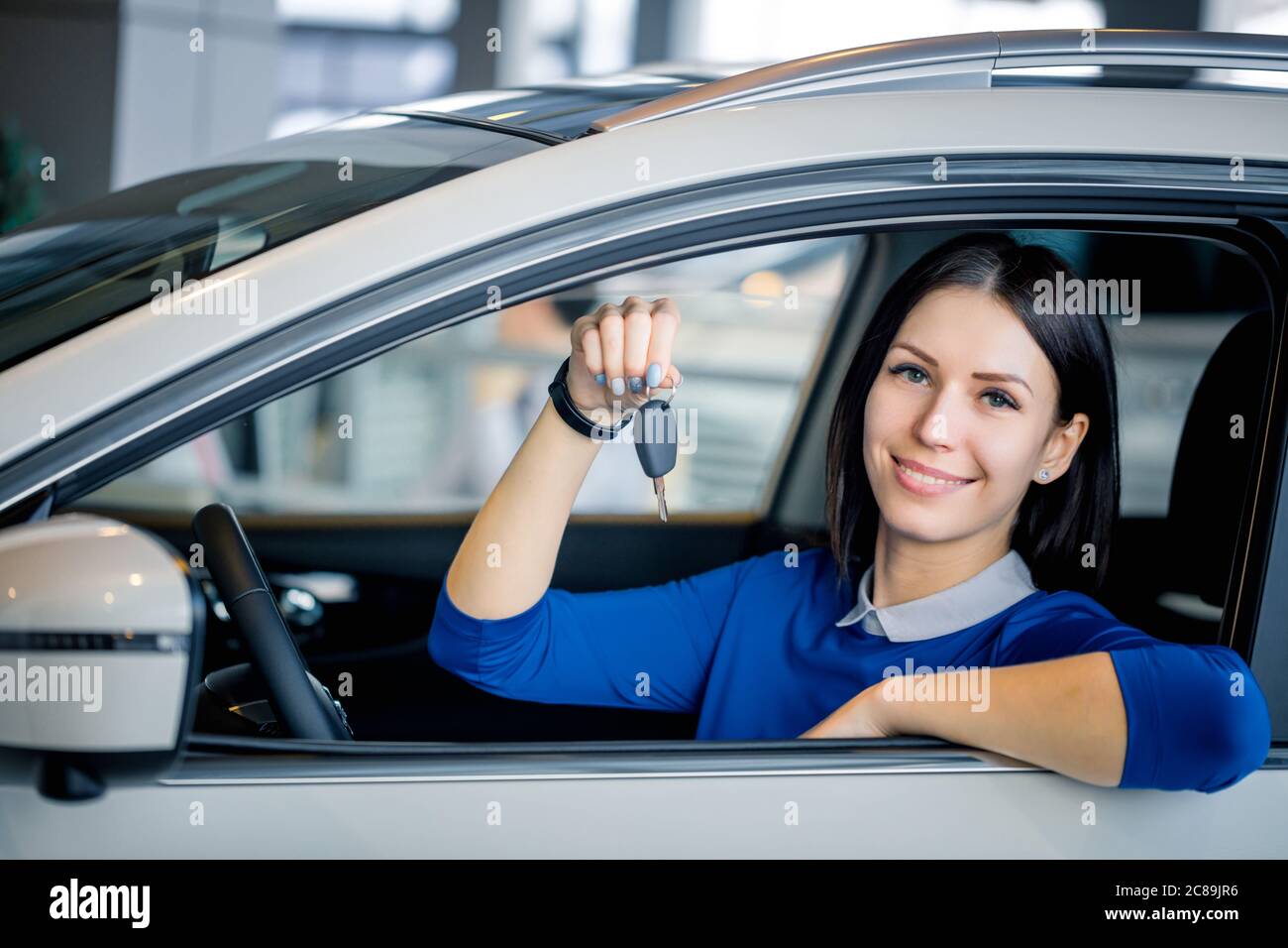 Smiling sales woman presenting the key of new car in dealership ...