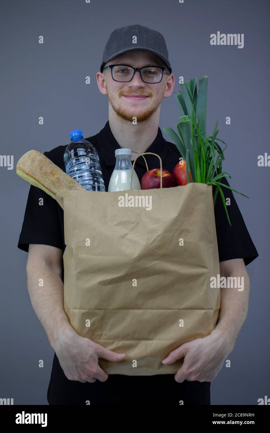 Handsome delivery man carrying paper bag of grocery food and drink from ...