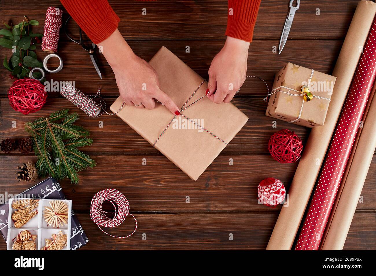 Female hands tie a unprepared gift wrapped in kraft paper with string ...