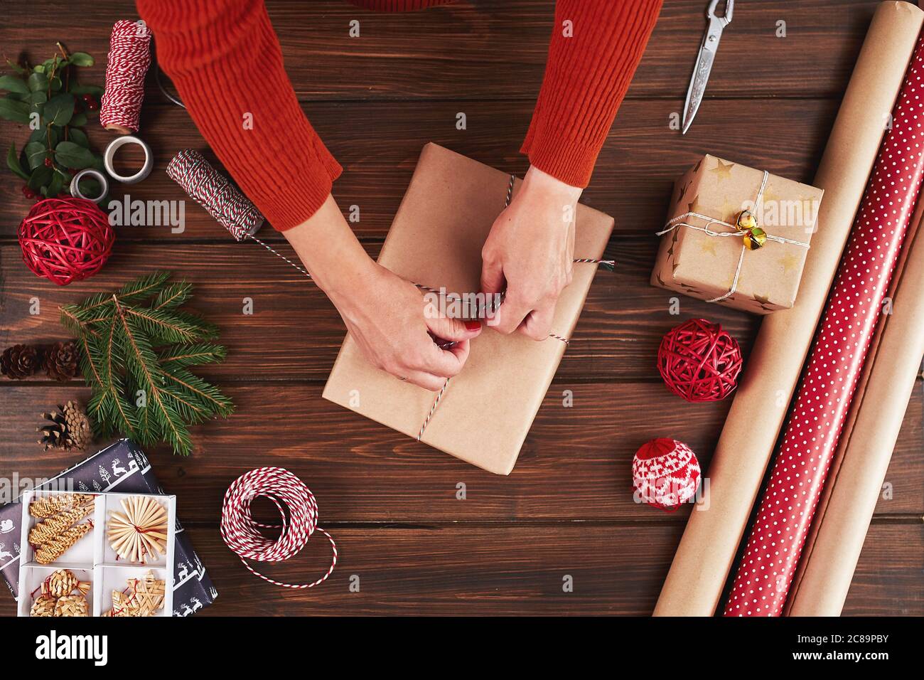 Female hands tie a unprepared gift wrapped in kraft paper with string ...