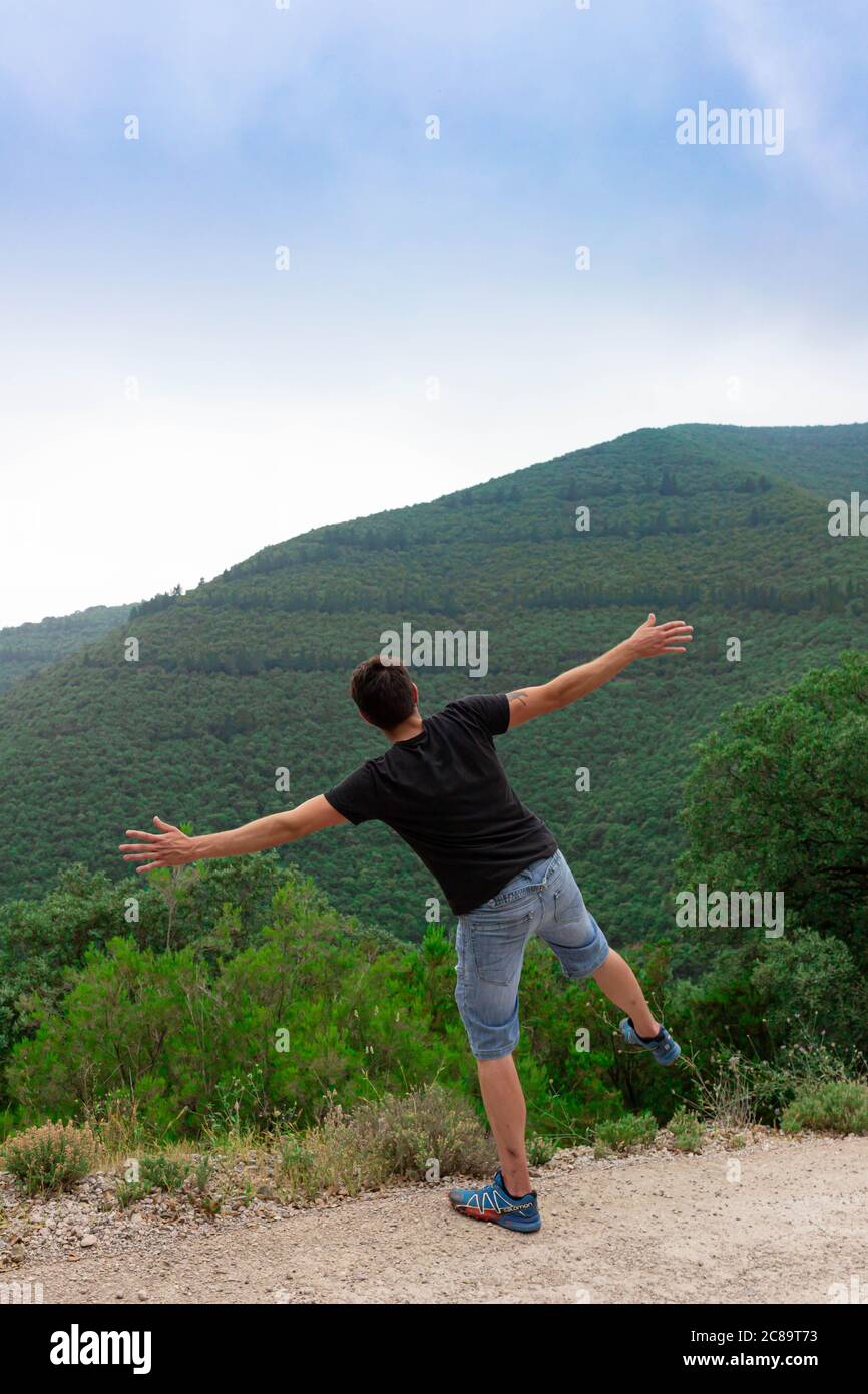 Vertical back view of a male having fun posing with a scenic hill ...