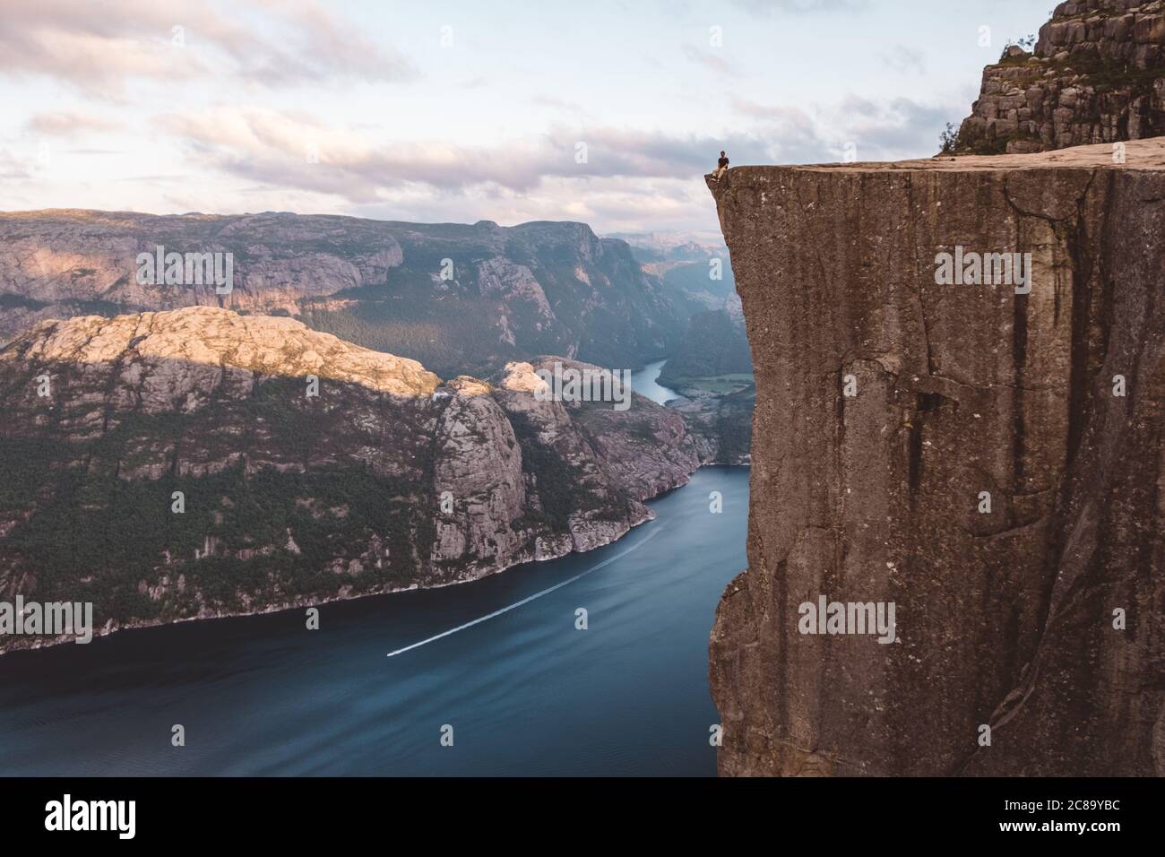 Man sitting on edge of cliff at fjords in Prekeistolen Norway Stock ...