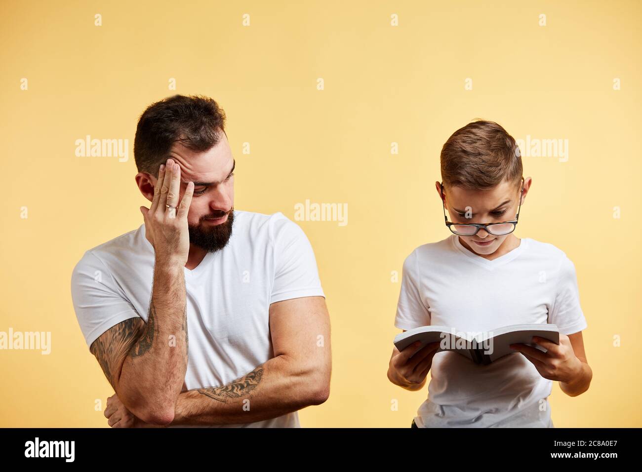 father incredulously looking at cute son reading book at yellow ...