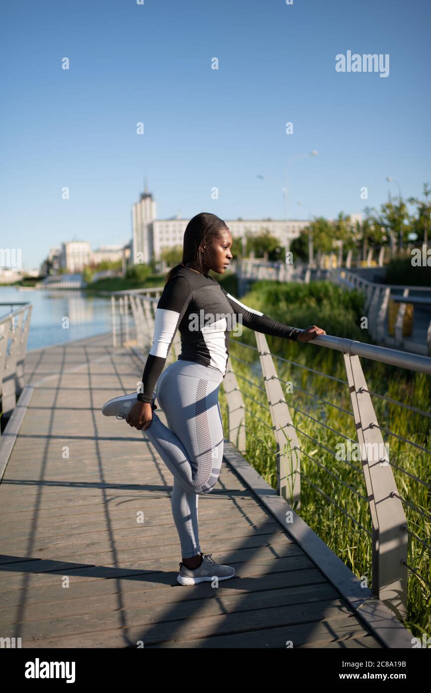 Side view of black runner stretching leg during morning workout on quay ...
