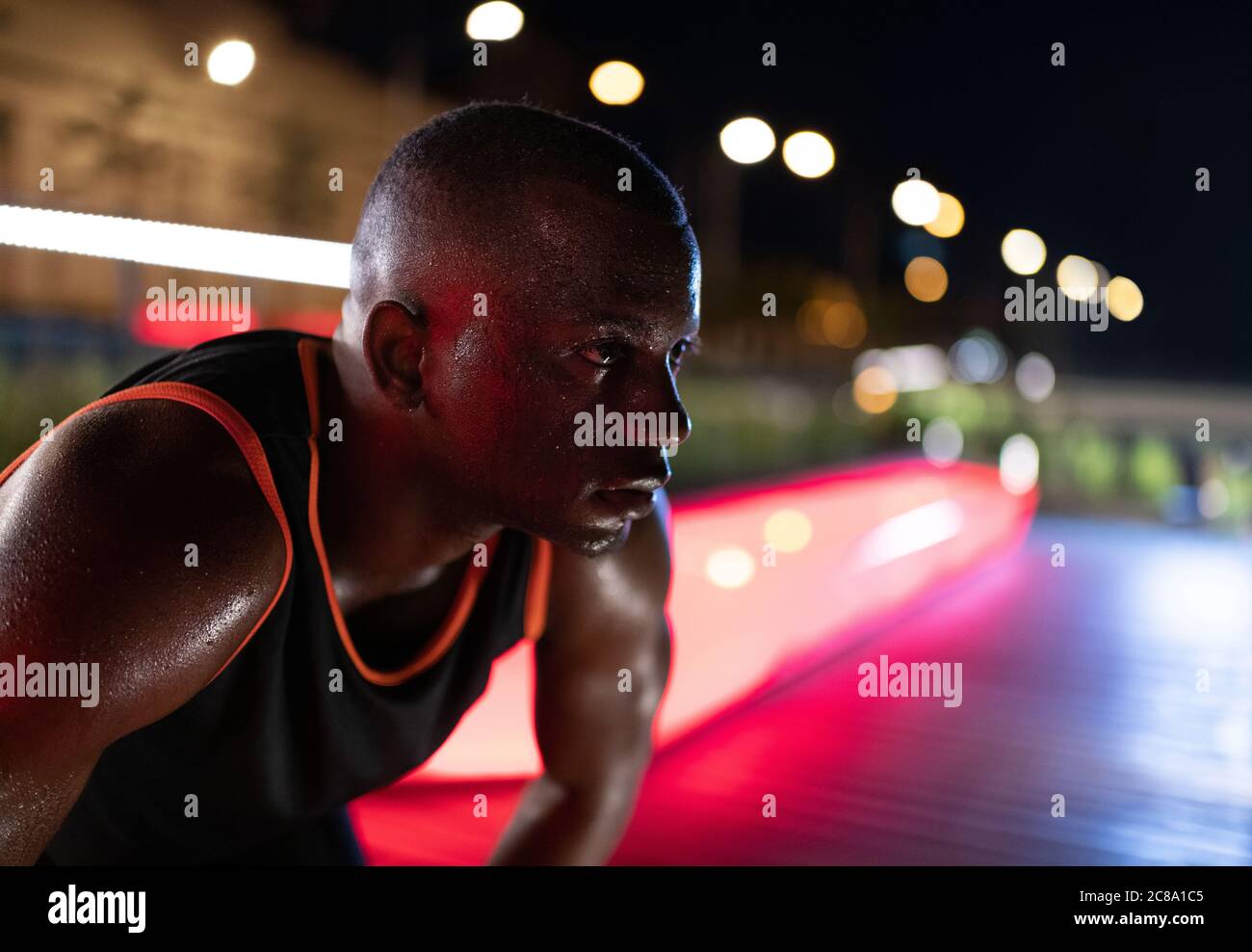 Tired black runner looking away and resting during training on night ...