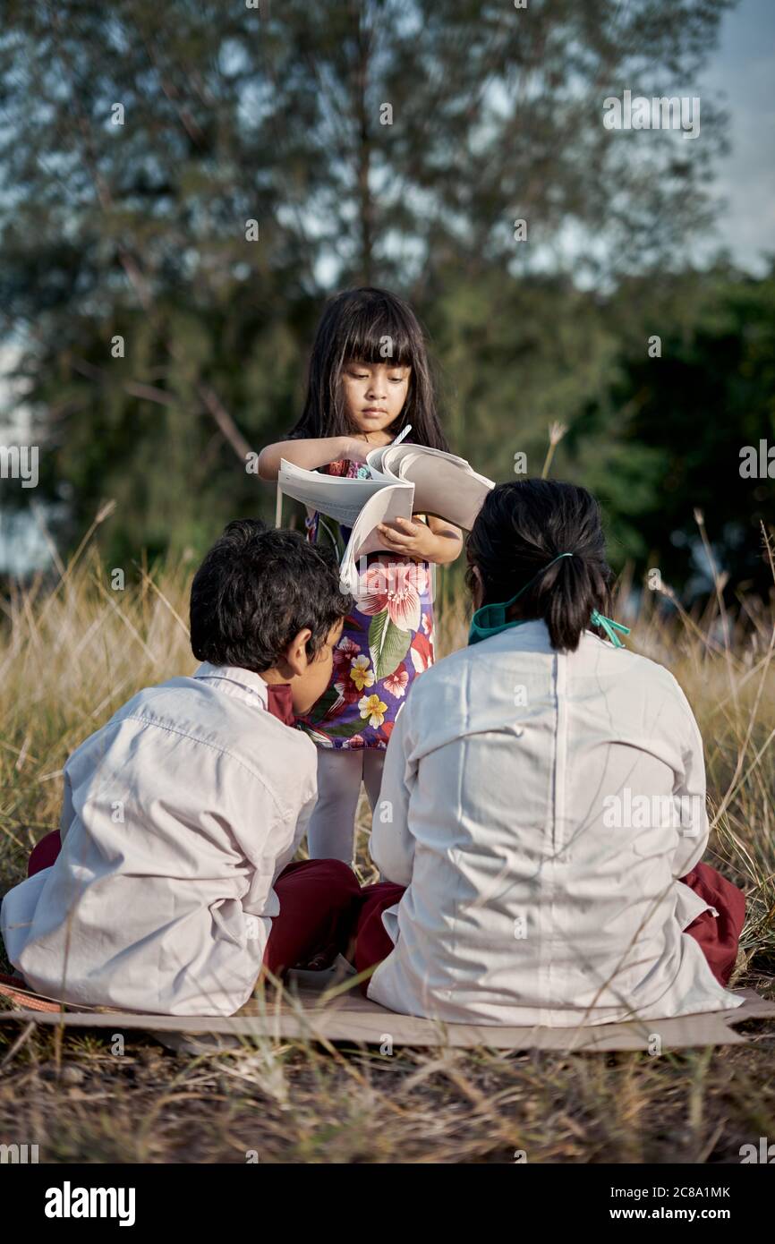 Happy little girl writing a book while her brother and sister doing ...