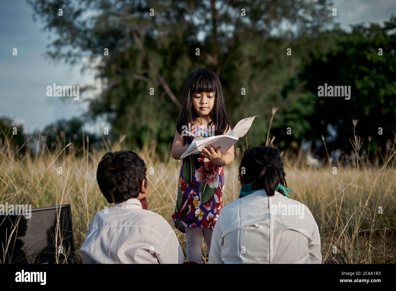 Happy little girl writing a book while her brother and sister doing ...