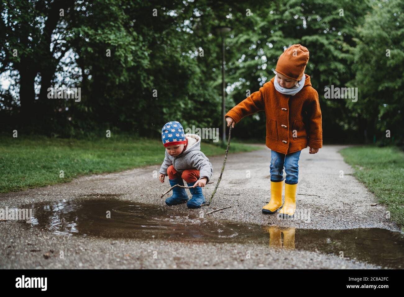Front view of young male kids playing with sticks in a puddle in park ...