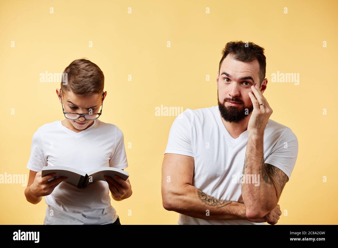 father incredulously looking at cute son reading book at yellow ...