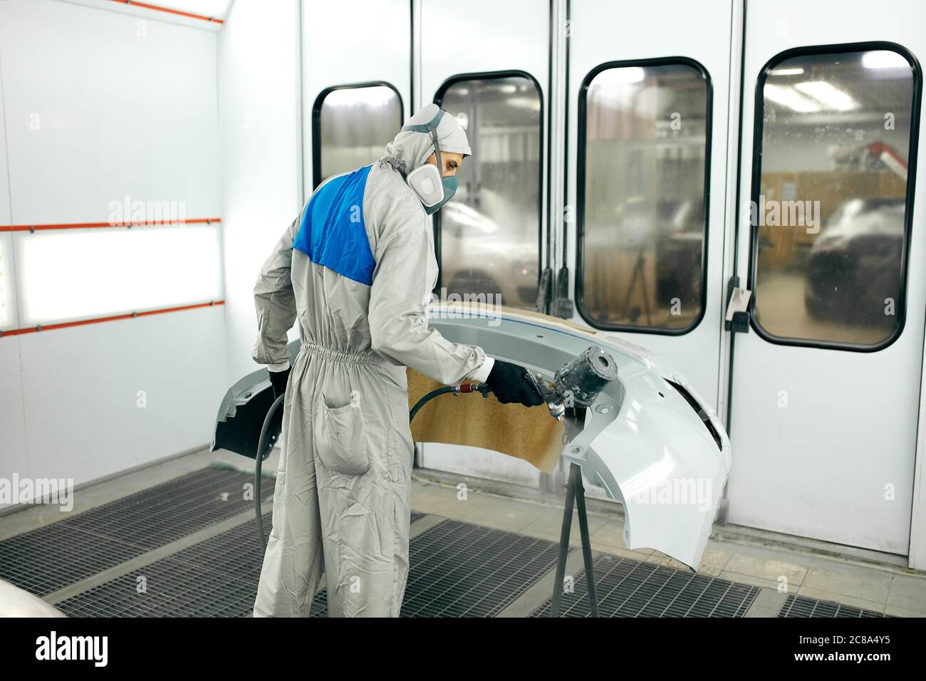 auto mechanic worker painting car bumper in paint chamber during repair ...