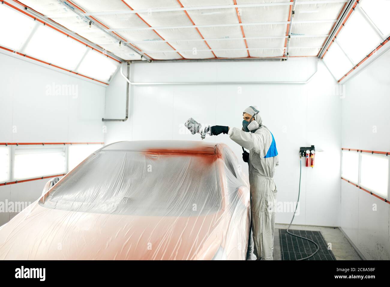 Man with protective clothes and mask painting car roof using compressor ...