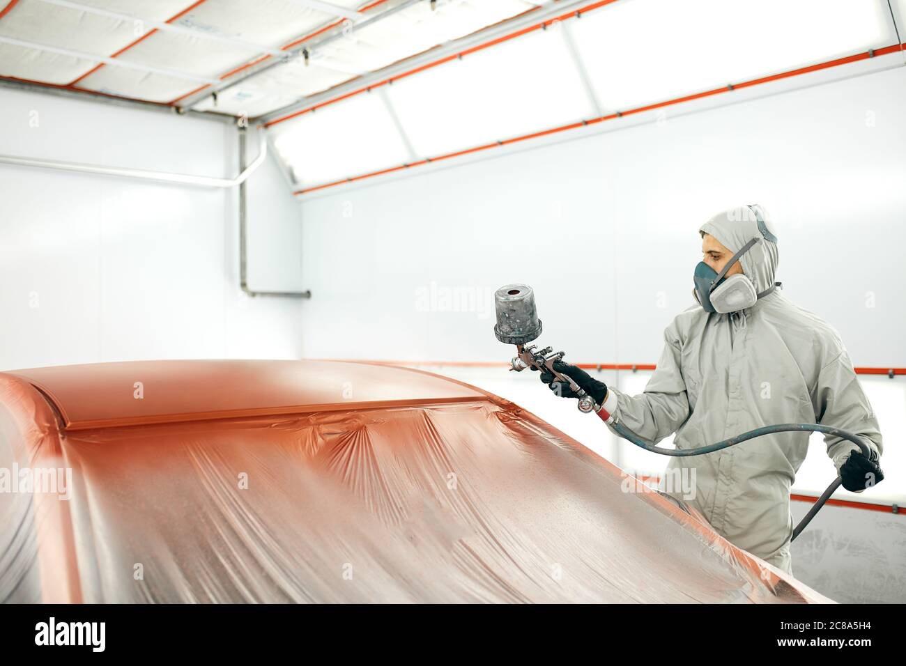 Man with protective clothes and mask painting car roof using compressor ...