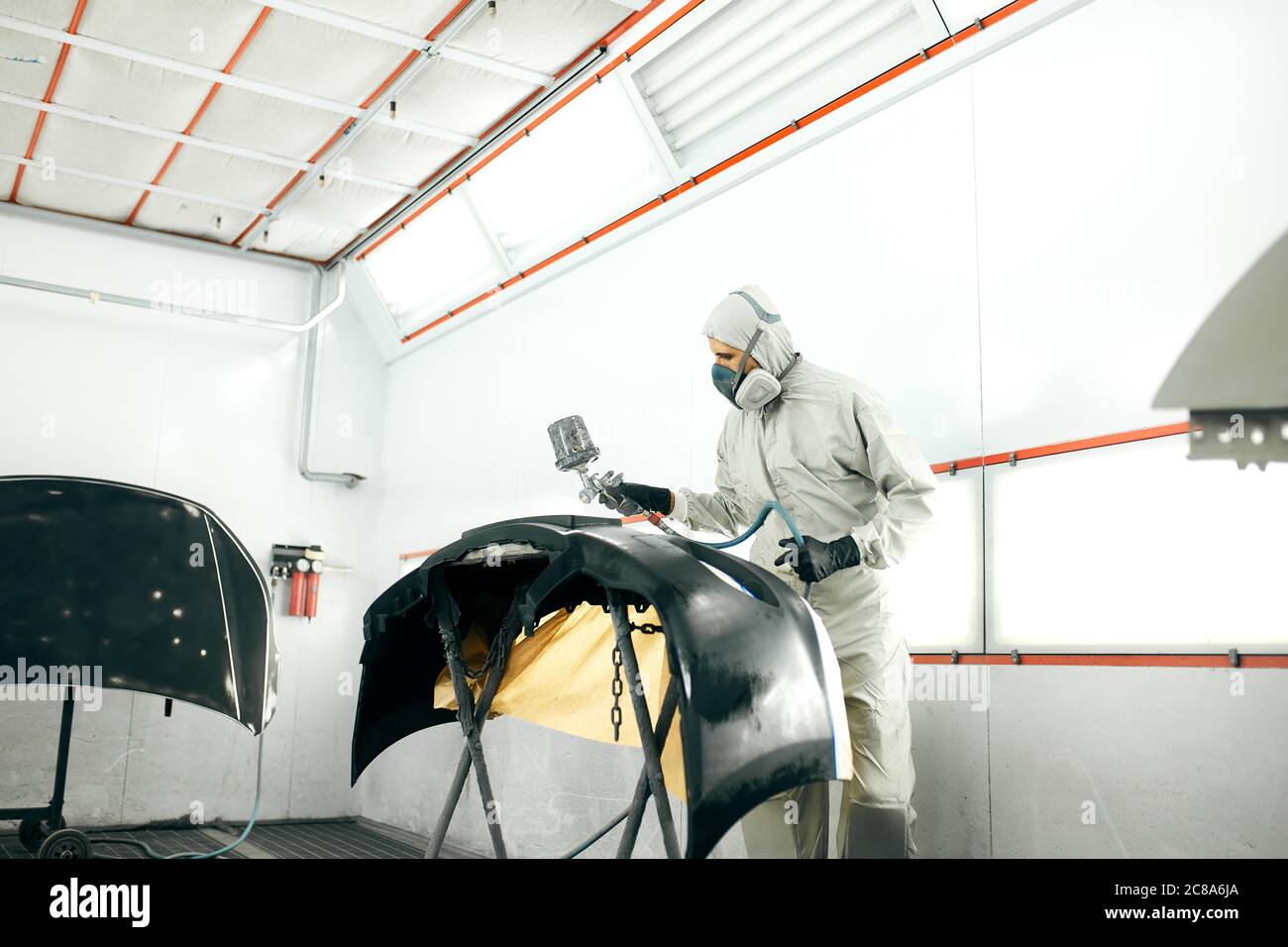 auto mechanic worker painting car bumper in paint chamber during repair ...