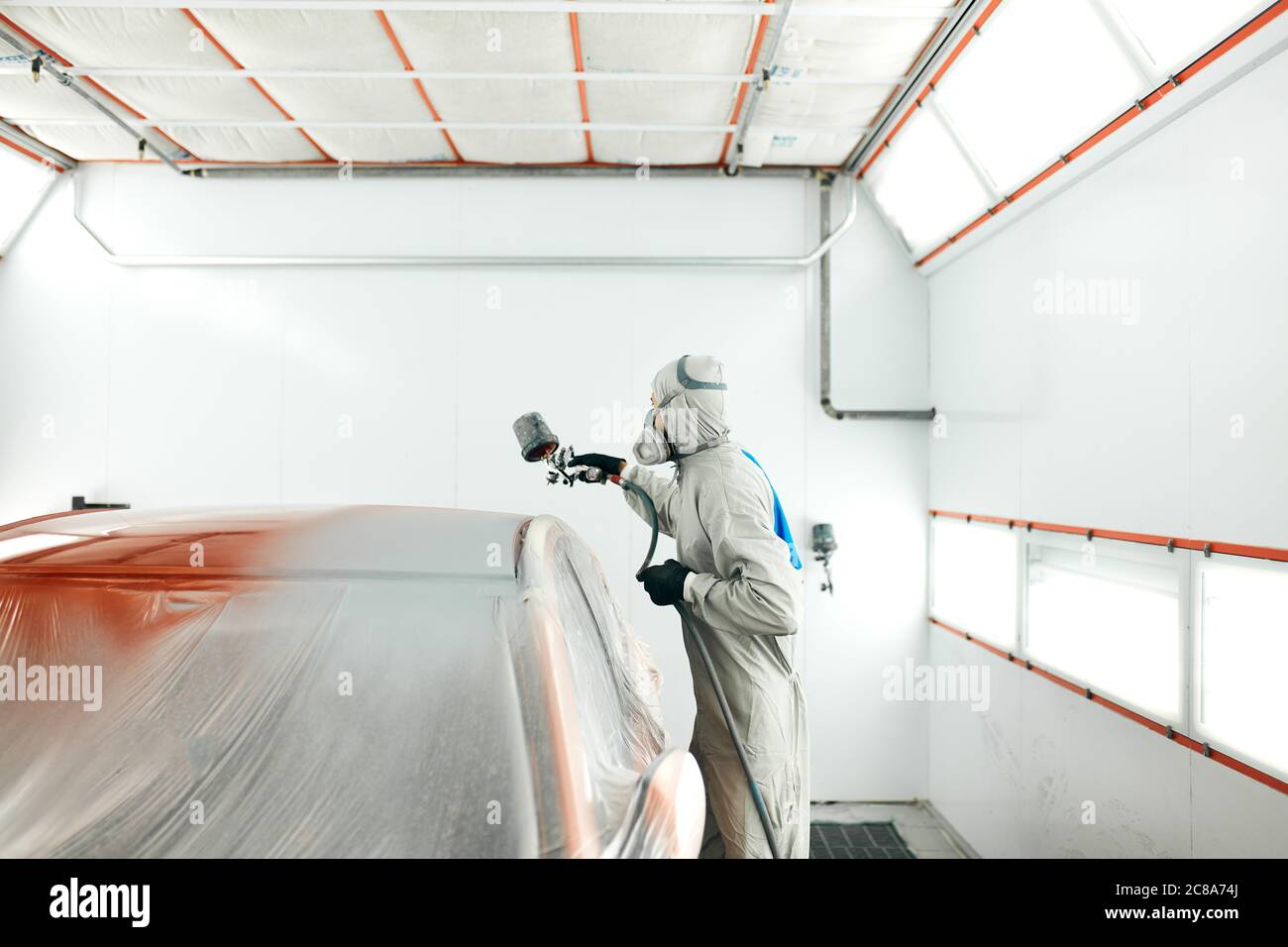 Man with protective clothes and mask painting car roof using compressor ...