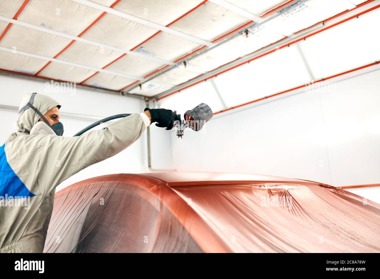 Man with protective clothes and mask painting car roof using compressor ...