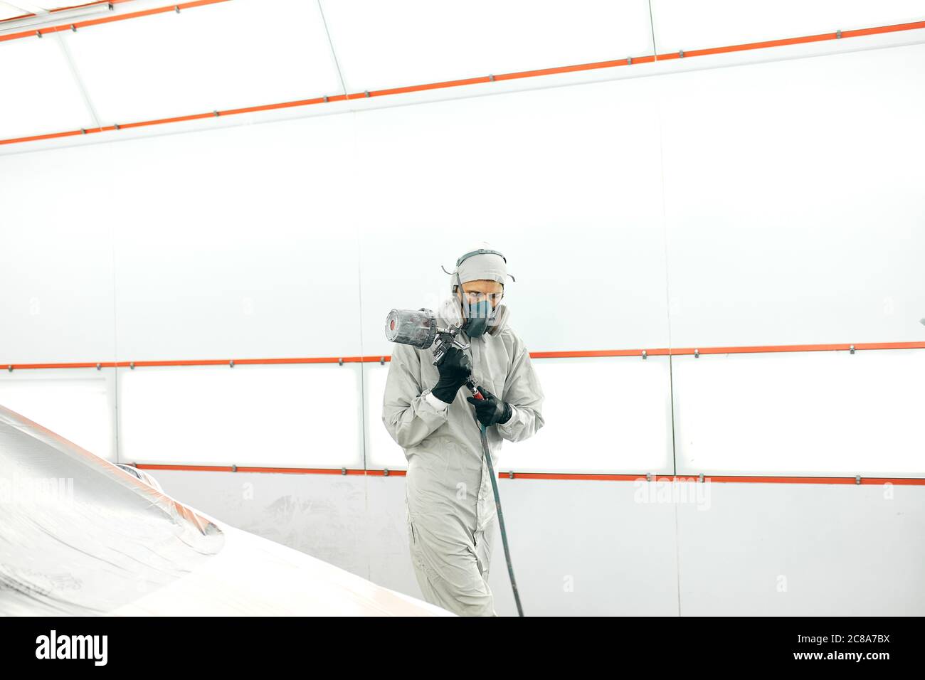 Man with protective clothes and mask painting car roof using compressor ...