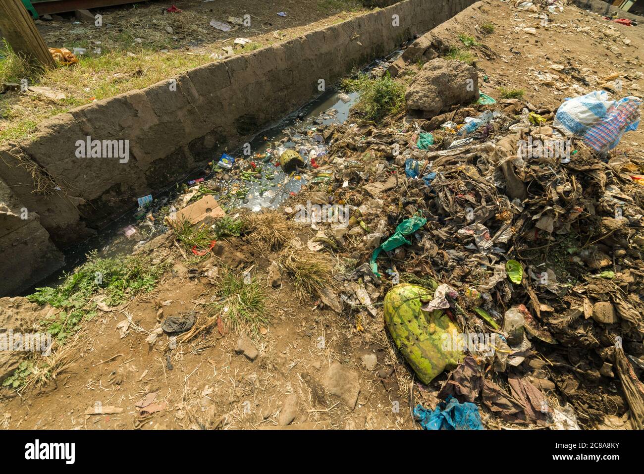 An open sewer filled with rubbish by the side of a dirt alley ...