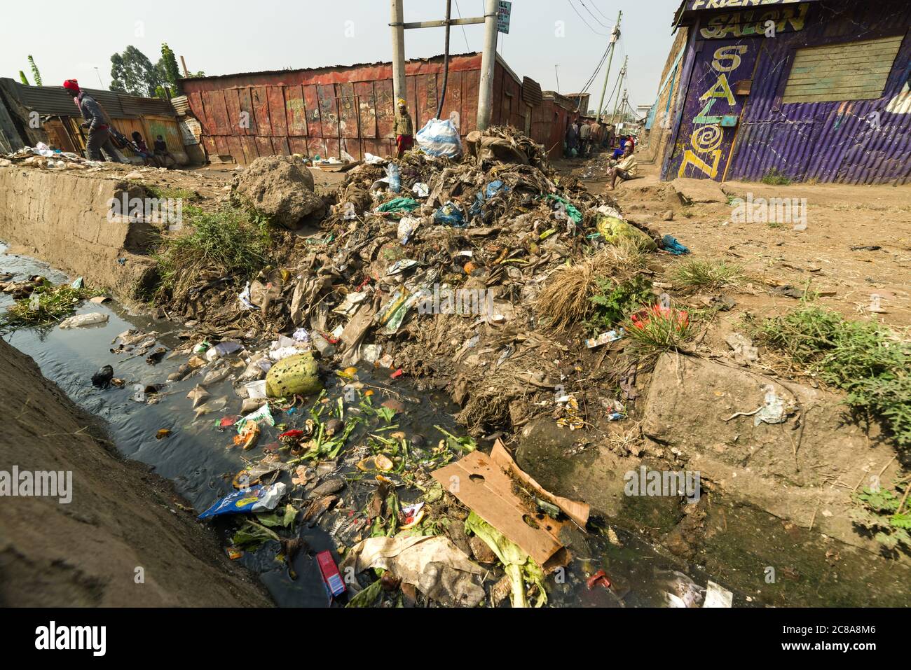 An open sewer filled with rubbish by the side of a dirt alley ...