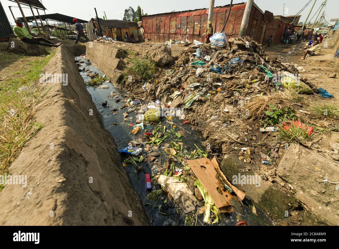 An open sewer filled with rubbish by the side of a dirt alley ...