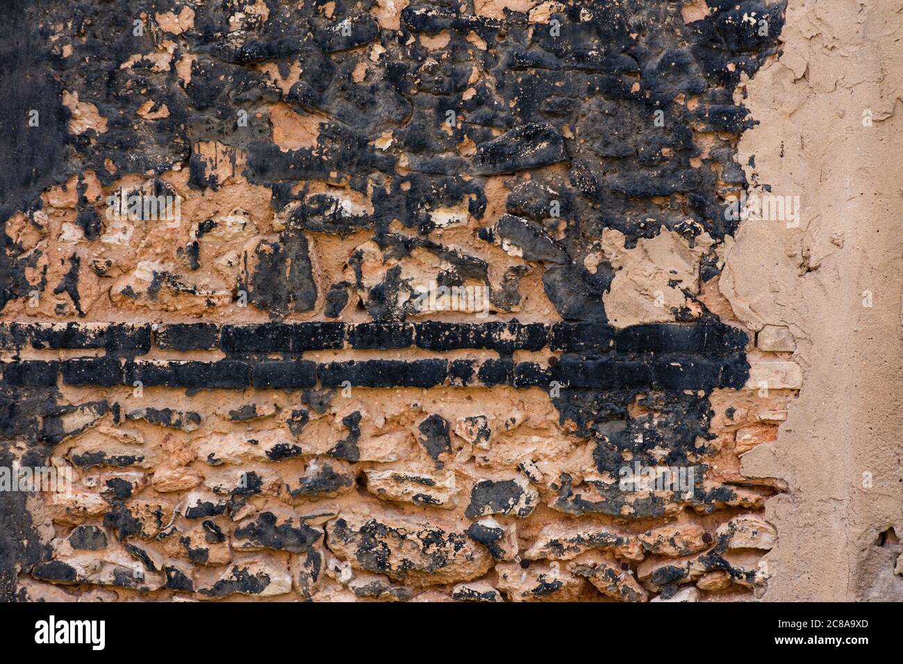 Wall of stones and clay bricks of an old house stained with black paint ...