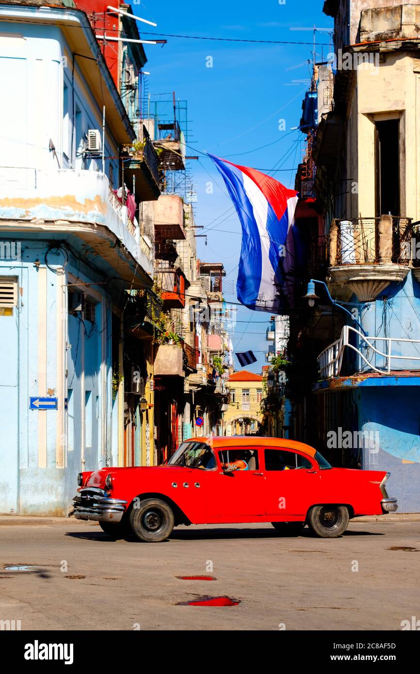 Urban scene with cuban flags, antique cars, people and aged buildings ...