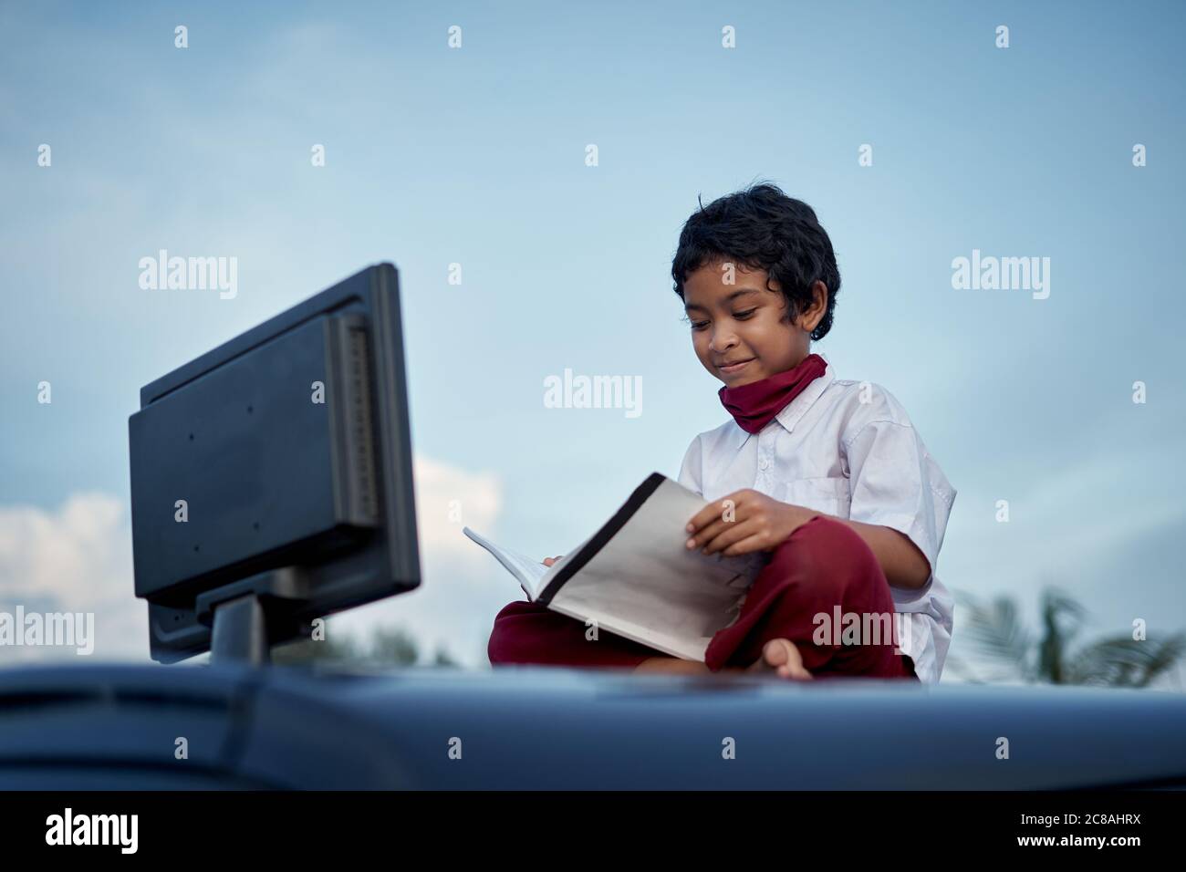 Schoolboy doing homework using computer on top of car roof, New Normal ...
