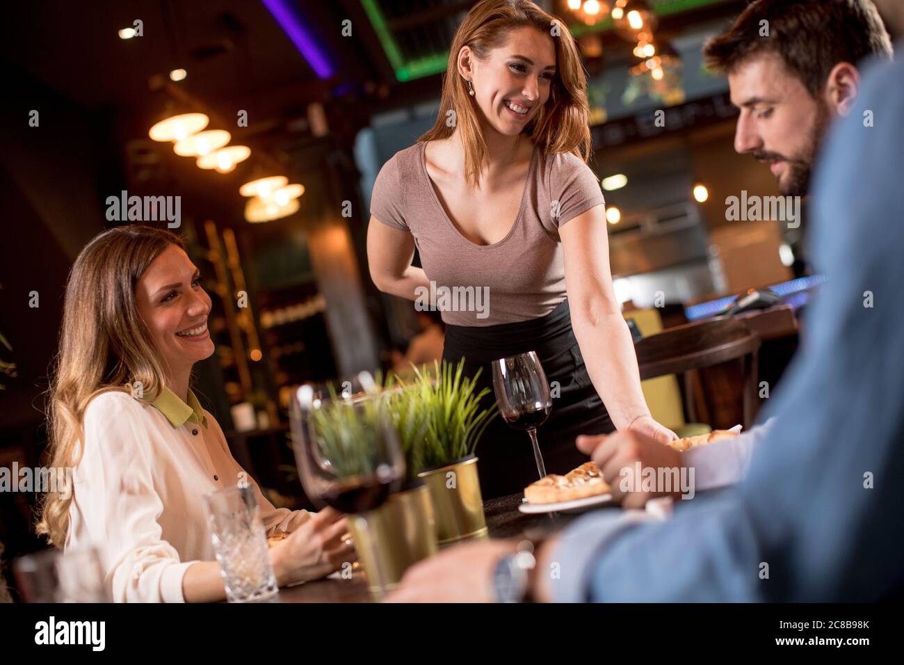Pretty waiter woman serving group of friends with food in the ...