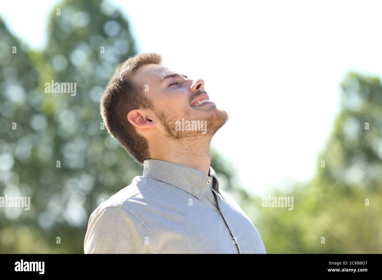 Happy man breathing fresh air standing on a park outdoors with green ...